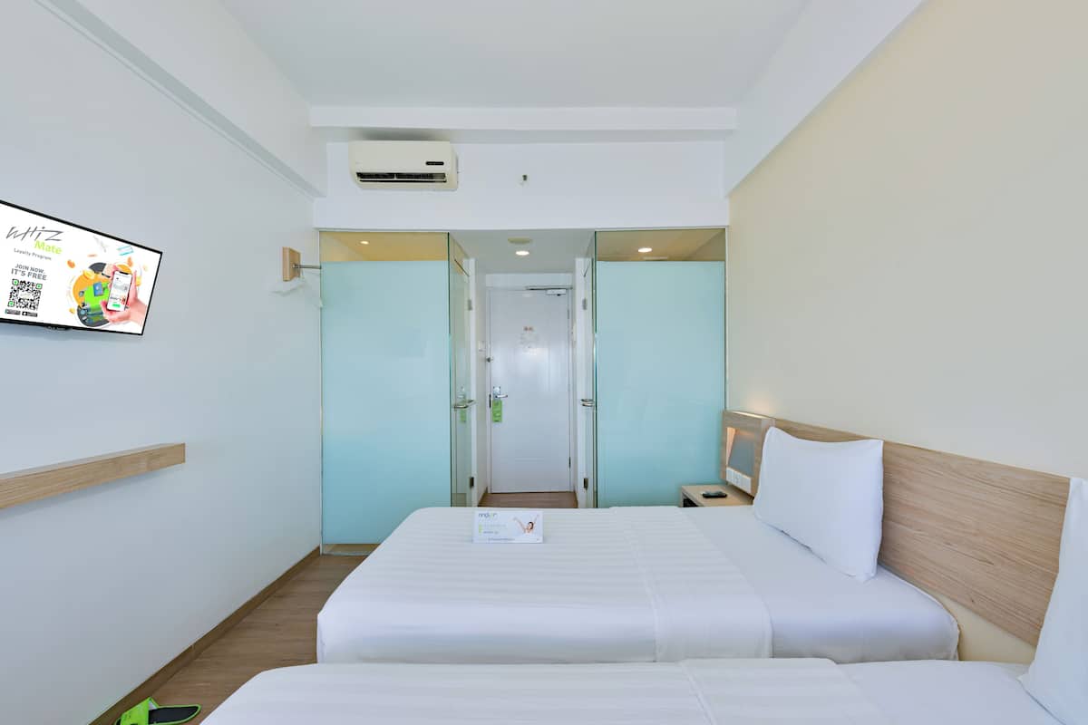 Quarto de hotel com cama, mesa de cabeceira, televisão presa à parede e porta que dá para outro espaço.