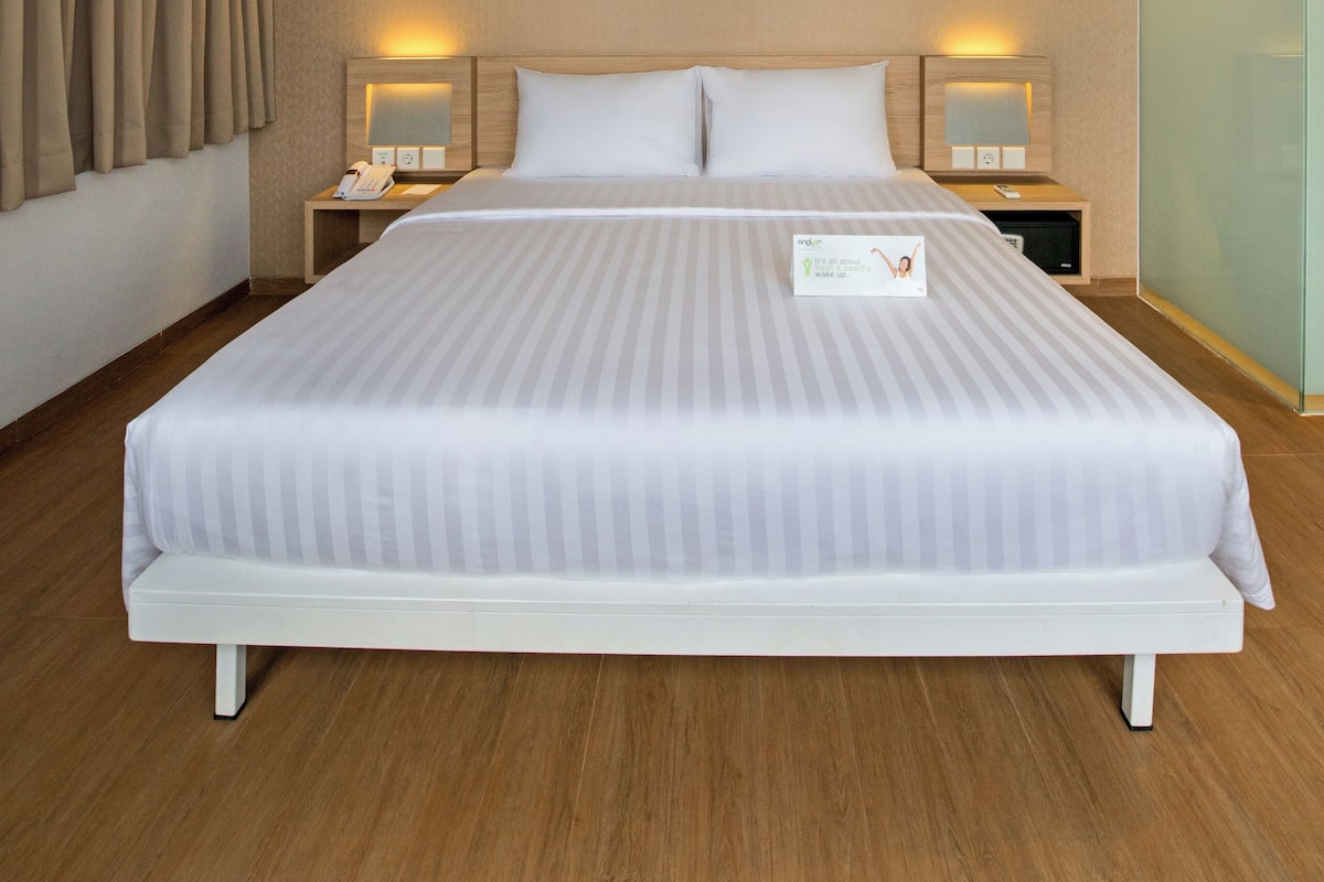 Quarto de hotel com uma cama grande, duas mesas de cabeceira com luminárias, um espelho e uma luminária no teto vermelha.