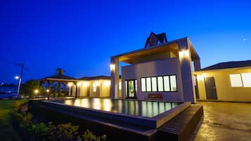 Uma casa moderna com piscina, um alpendre coberto e fachada bem iluminada ao anoitecer.