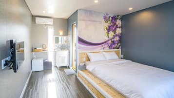 Quarto de hotel moderno com cama de madeira, toucador com espelho, frigorífico pequeno e ar condicionado fixado na parede.