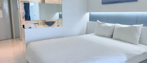 Quarto de hotel moderno com uma cama grande, mesa de cabeceira, espelho e um quadro na parede.
