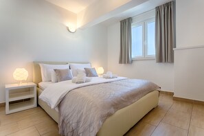 Quarto bem arrumado com uma cama, mesas de cabeceira, abajur e uma janela com cortinas.