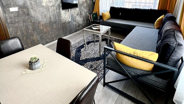 Uma sala de estar moderna com um sofá, uma mesa de jantar e uma televisão fixada na parede.