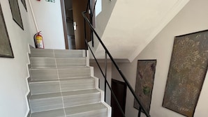 Uma escadaria com design moderno, um extintor de incêndio e uma porta que dá para outro cômodo.