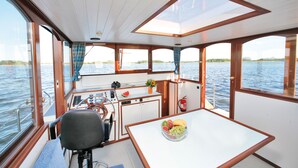 Interior de barco com área de refeições, cozinha e leme.