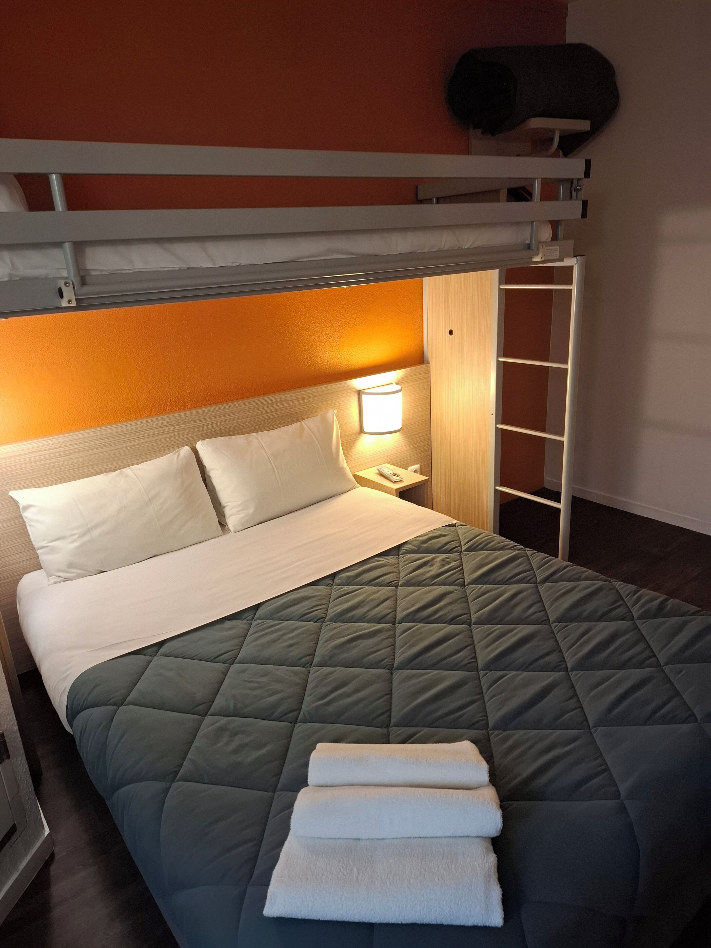 Uma cama beliche com colchão acolchoado verde, almofadas brancas e uma mesa de cabeceira com abajur.