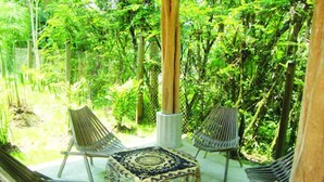 Uma área externa com assentos de metal e uma mesa estampada, cercada por vegetação exuberante.