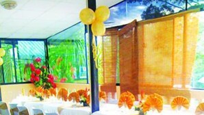 Uma sala de banquetes com mesas e cadeiras brancas, cada uma com um laço marrom.