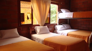 Quarto com duas camas de solteiro e uma cama beliche, tudo com roupa de cama branca e colchas laranja.