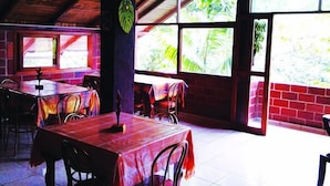 Um restaurante com teto de madeira rústica, grandes janelas com vista para o verde e piso de azulejos.