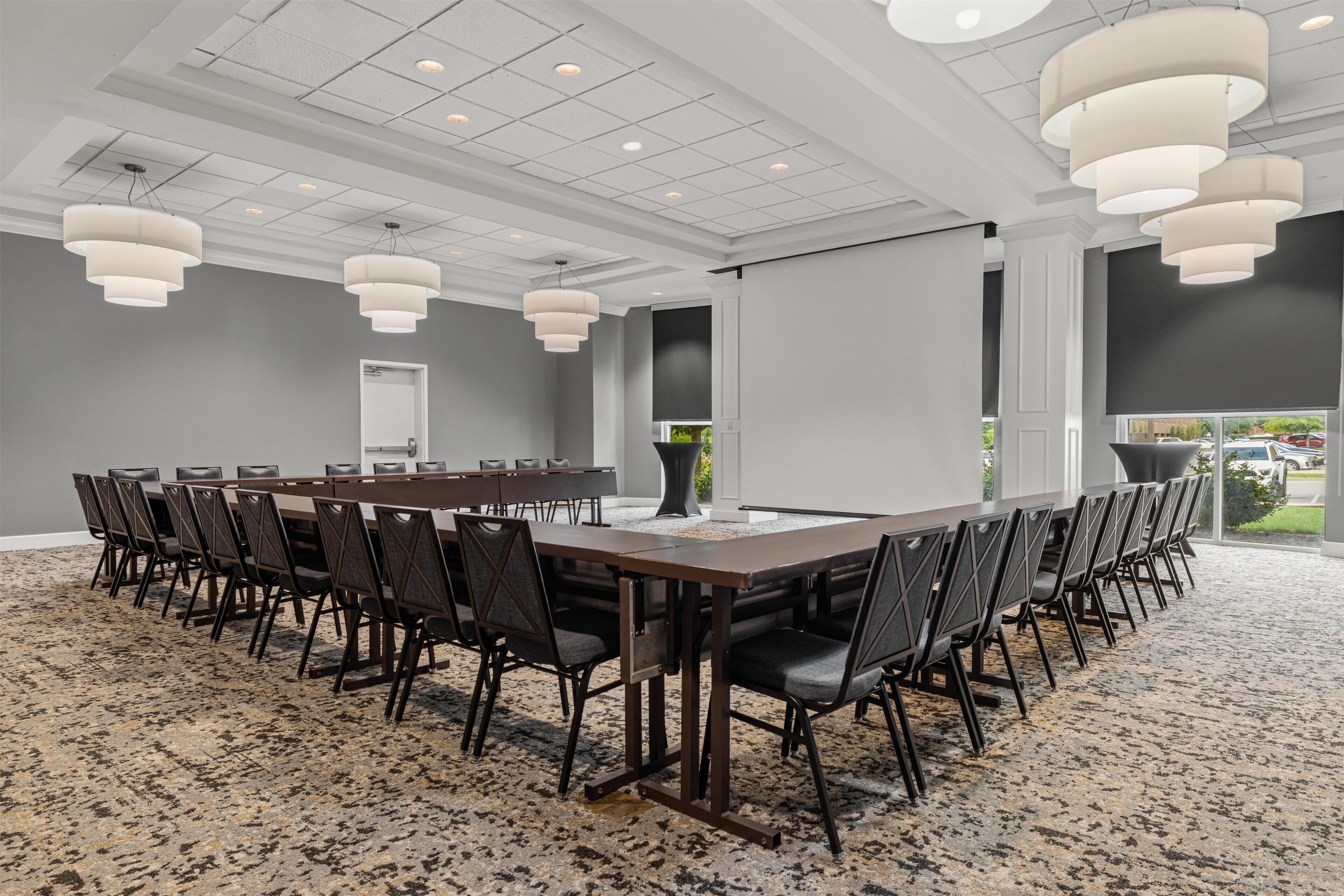 Uma sala de conferências com uma mesa comprida, cadeiras e uma tela de projeção.