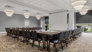 Uma sala de conferências com uma mesa comprida, cadeiras e uma tela de projeção.