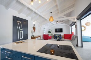 Uma cozinha moderna com uma ilha central, uma área de jantar com cadeiras vermelhas e um ventilador de teto.