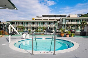 Área de piscina com profundidade de 90 centímetros e placa indicando 0,9 metros de largura, cercada por um edifício com várias varandas e uma galeria coberta.