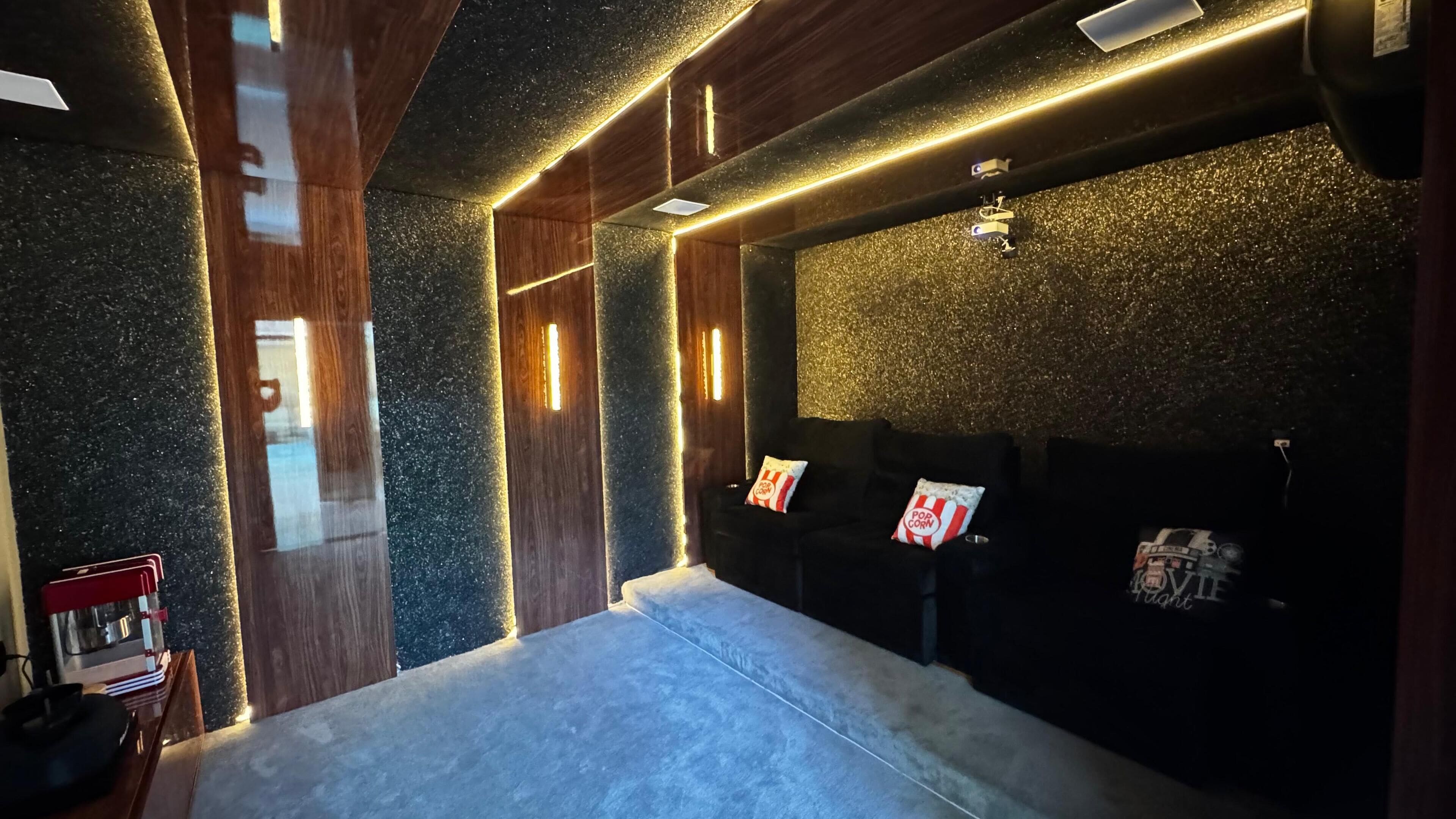 Quarto moderno com parede escura e texturizada, vigas de madeira no teto e um espaço de estar com sofá e almofadas.