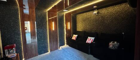 Quarto moderno com parede escura e texturizada, vigas de madeira no teto e um espaço de estar com sofá e almofadas.
