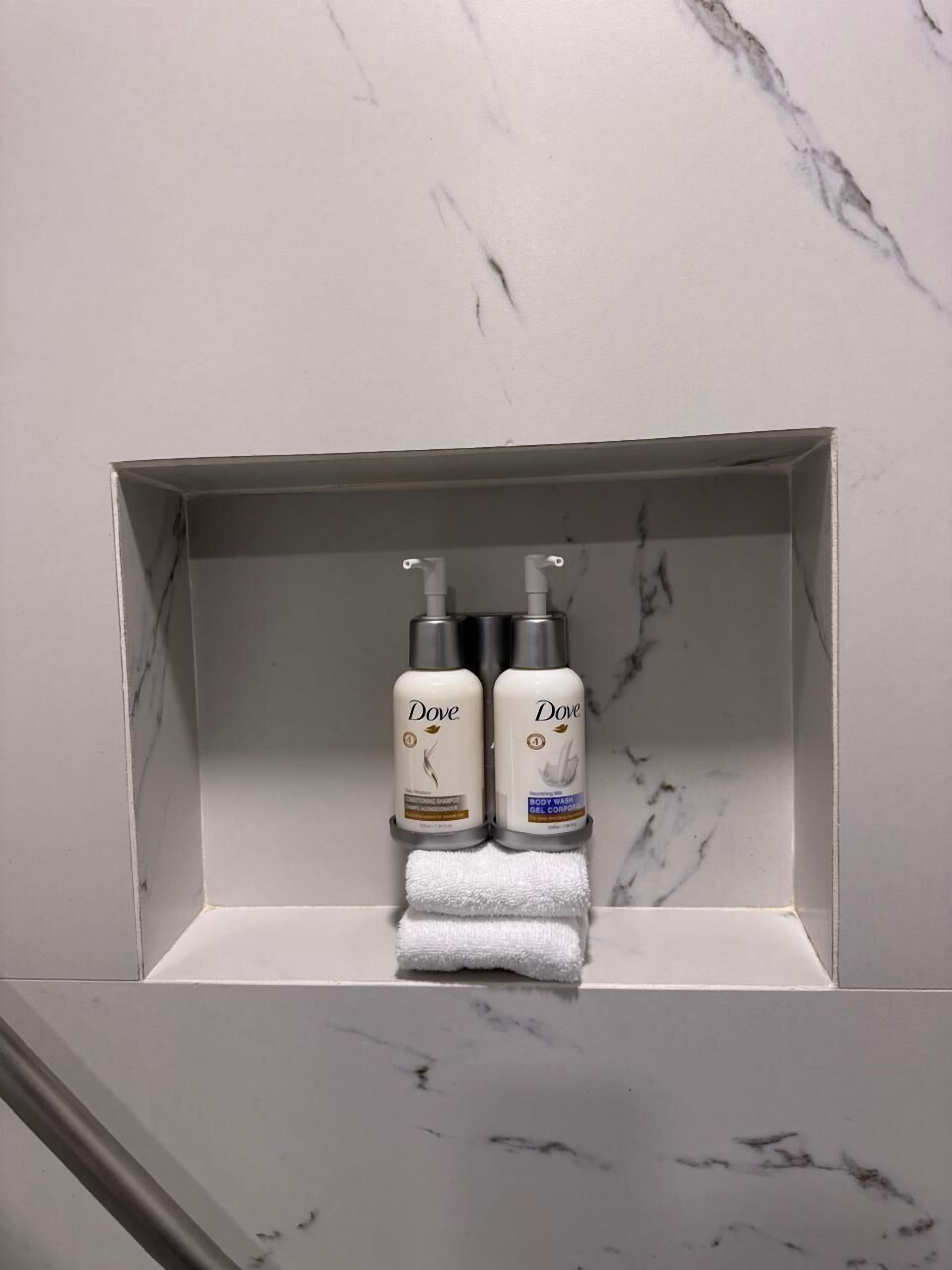 Uma prateleira de mármore com frascos de Dove de hidratante corporal e shampoo.
