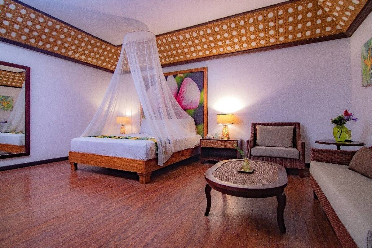 Quarto com cama, poltrona, sofá, mesa de cabeceira, abajur e espelho.