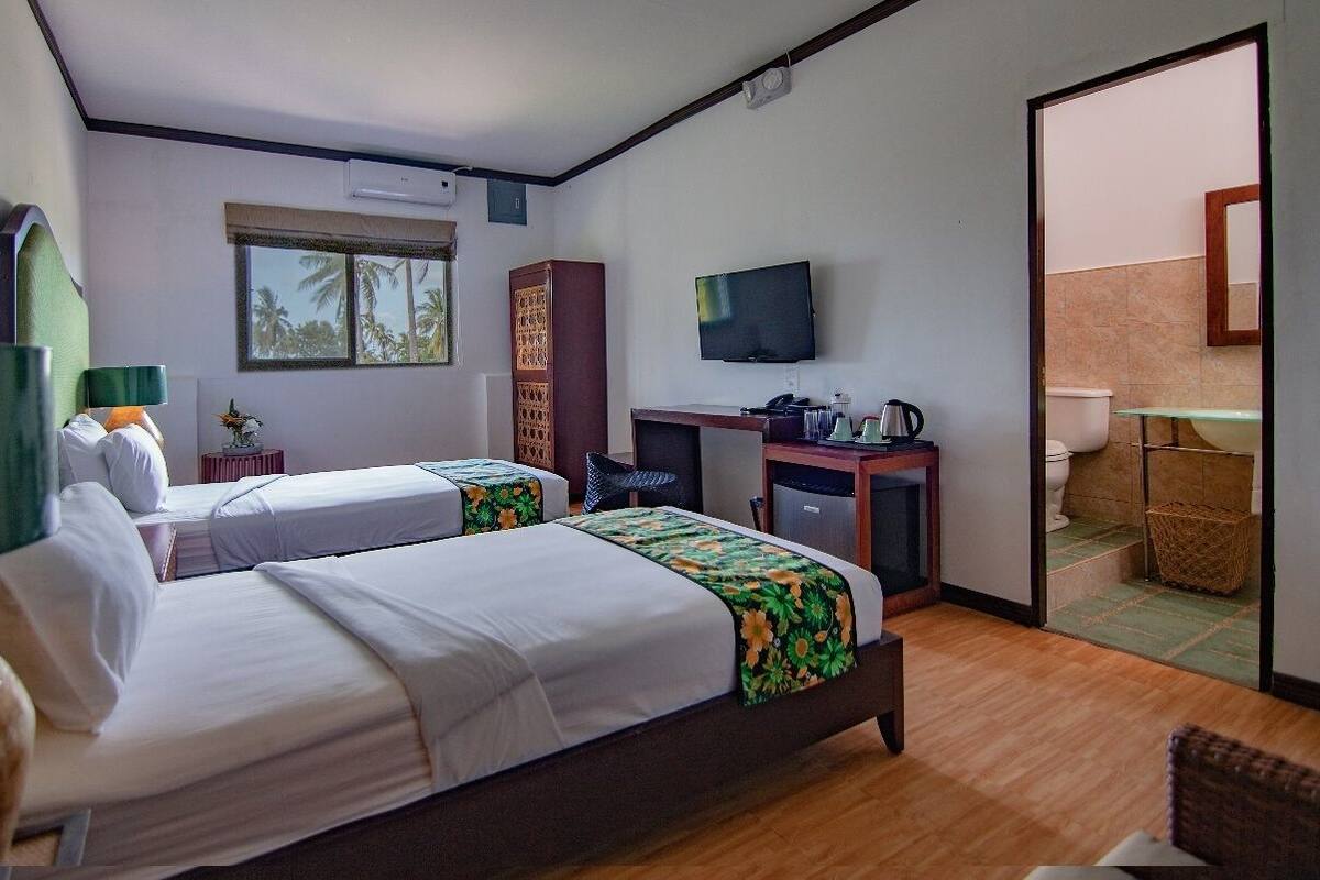 Quarto de hotel com duas camas, uma escrivaninha, uma televisão e um banheiro.