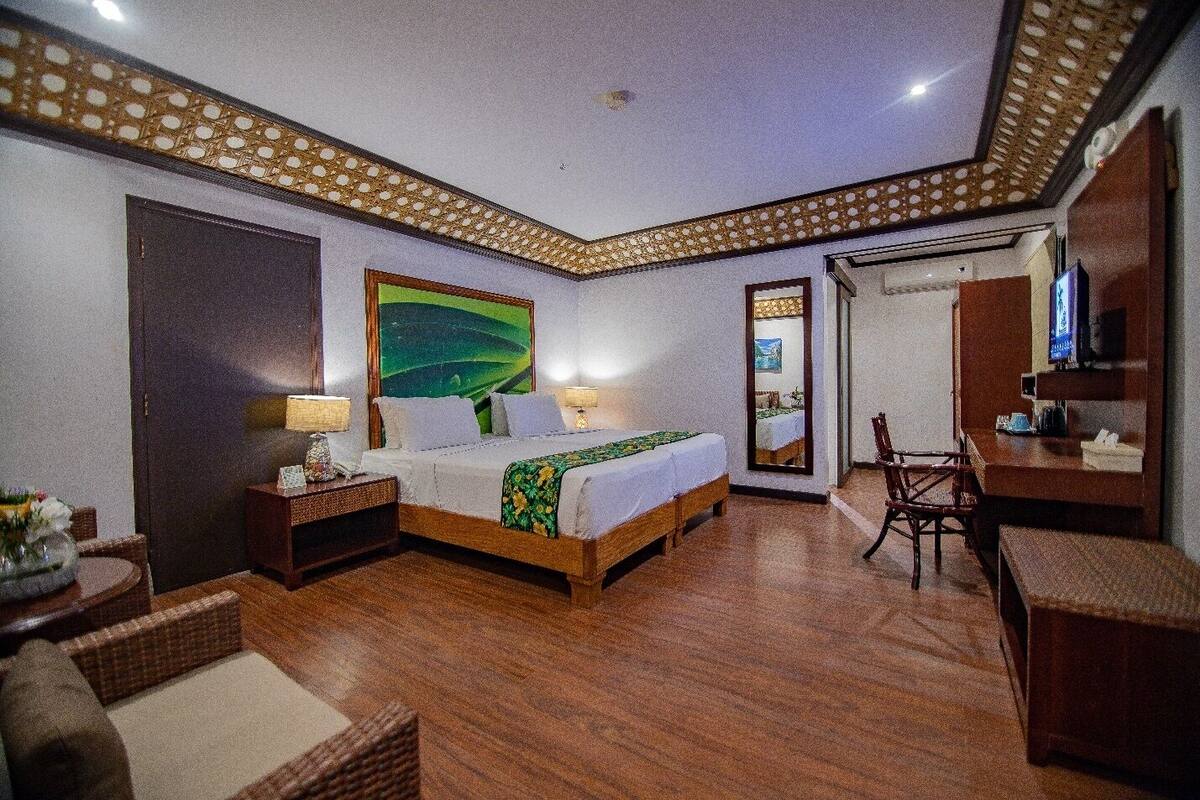 Quarto de hotel com cama, mesas de cabeceira, uma cadeira, escrivaninha e televisão.