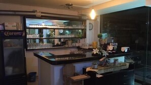Uma área de bar com geladeira, prateleiras com copos e um balcão com um banquinho.
