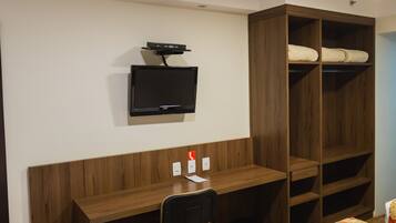 Quarto de hotel com escrivaninha de madeira, televisão fixada na parede, beliche com cabeceira de madeira e duas camas com colchas floridas.