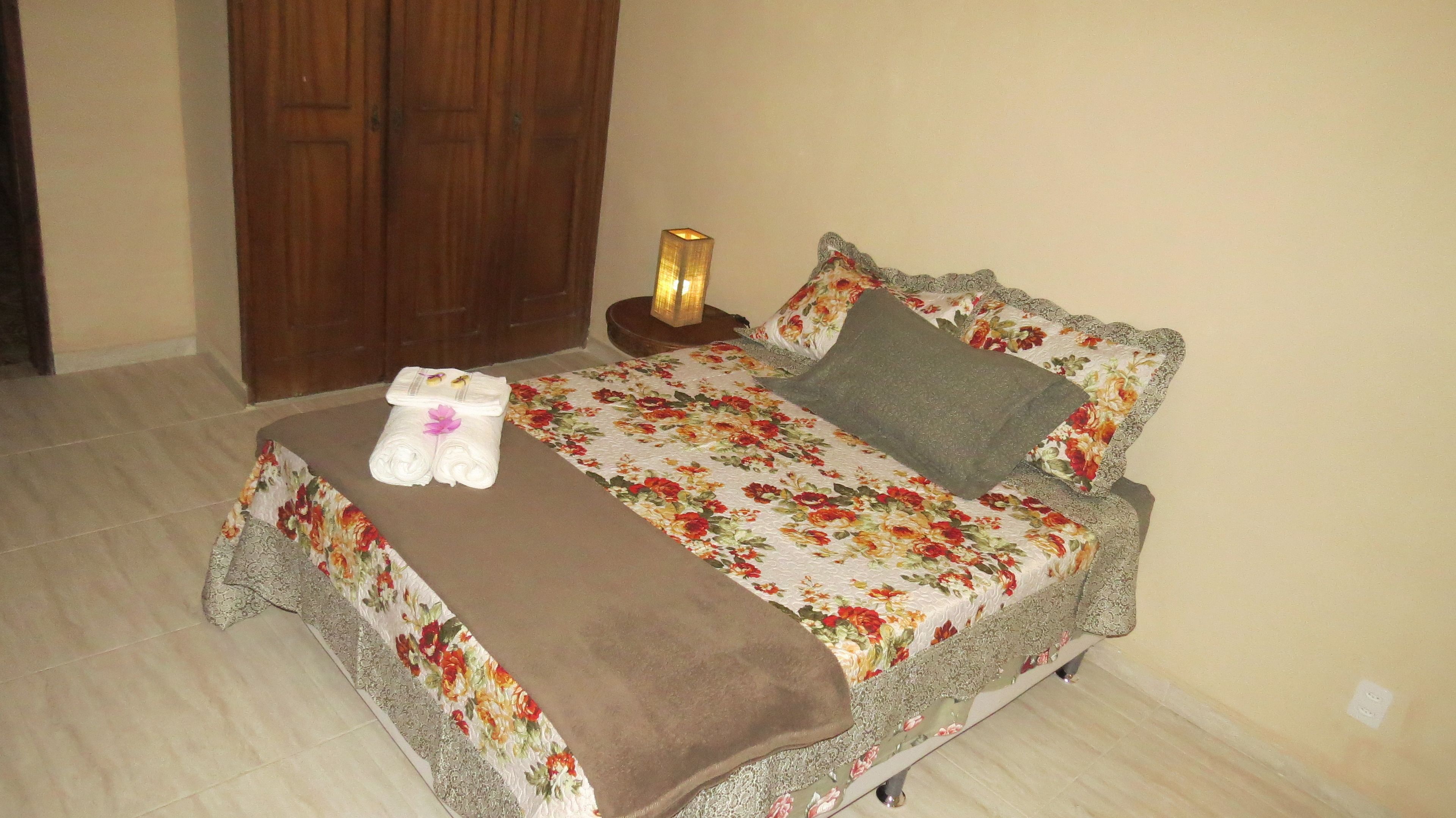 Uma cama com roupa de cama floral, um cobertor marrom e uma toalha dobrada com uma flor rosa.