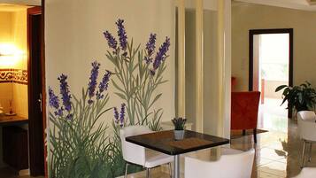 Quarto de hotel moderno com área de jantar, uma pequena mesa com cadeiras, uma planta em vaso e vista para o exterior.