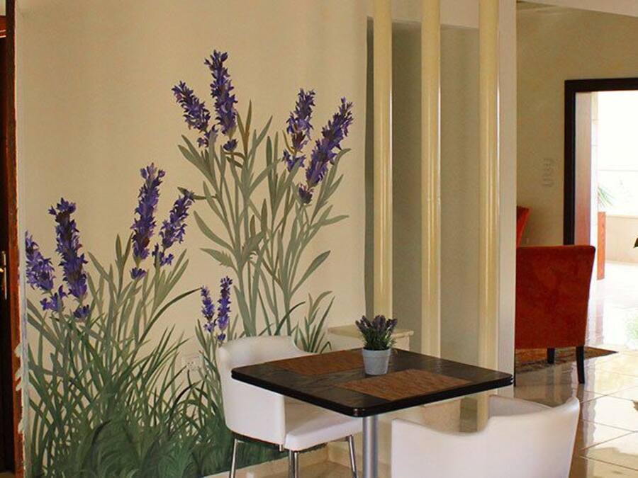 Quarto de hotel moderno com área de jantar, uma pequena mesa com cadeiras, uma planta em vaso e vista para o exterior.