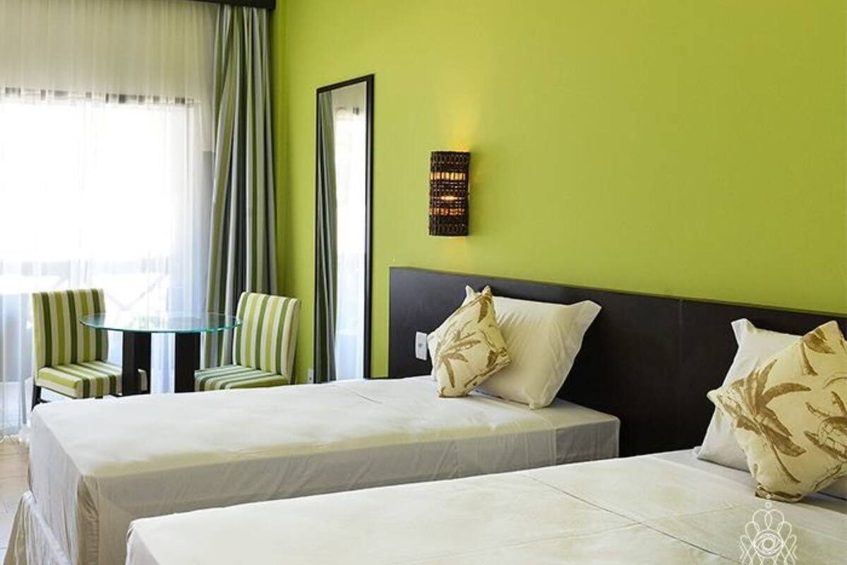 Quarto de hotel com duas camas, uma mesinha e cadeiras.
