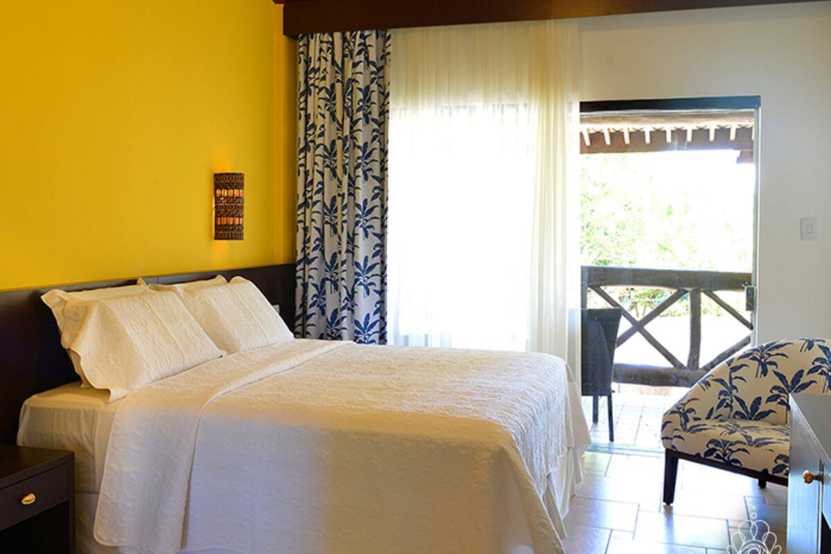 Quarto com cama, cadeira, teto de madeira e janela com cortinas.