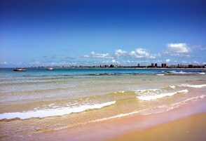 Na praia, areia branca, espreguiçadeiras, prática de windsurfe 