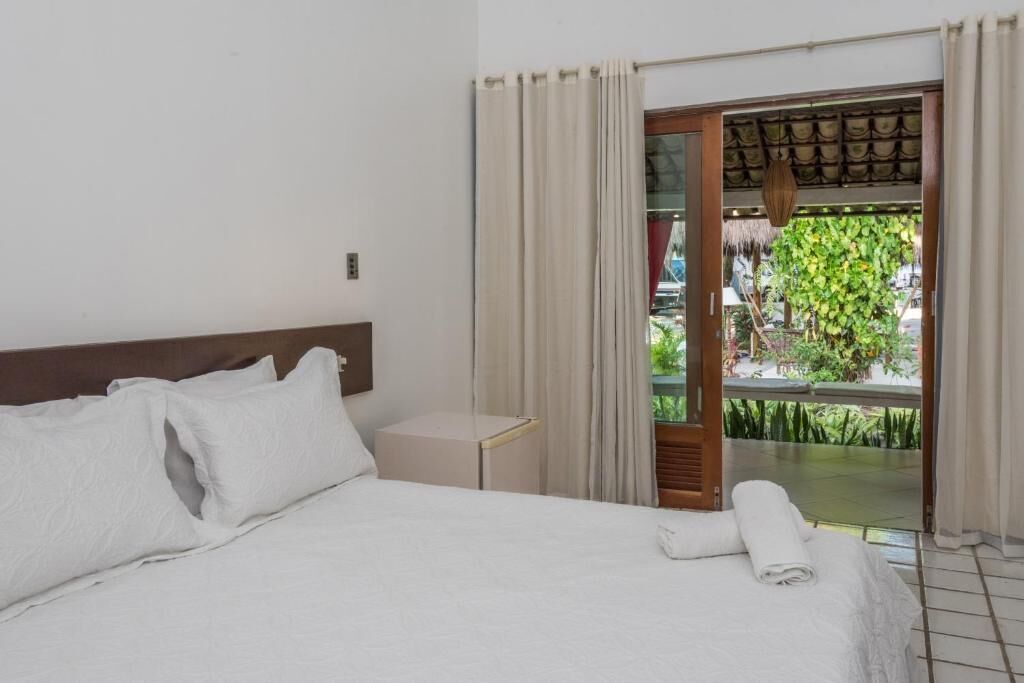 Quarto de hotel com cama, mesa de cabeceira e vista para um jardim através de uma porta de vidro.
