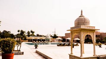 Um pátio com piscina, um gazebo e um edifício com cúpulas ao fundo.