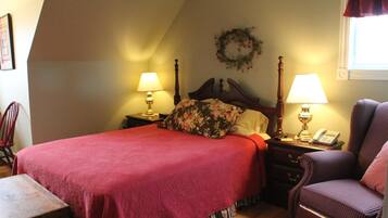Quarto com cama grande, duas mesas de cabeceira com abajures, uma cadeira, um baú de madeira e uma janela com cortinas.