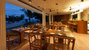Restaurante com mobiliário de madeira e vista para a praia ao entardecer.