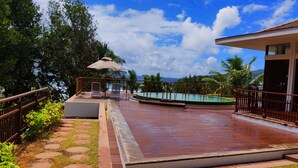 Um deck de madeira com piscina, cercado por palmeiras e vista para o oceano.