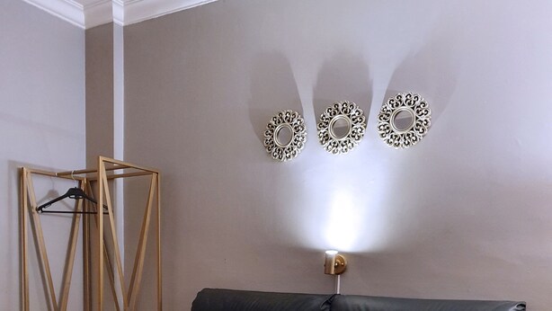Quarto com cama, cabideiro de madeira e arandelas decorativas.