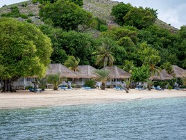 Um resort à beira-mar com cabanas de palha, espreguiçadeiras e uma praia de areia.