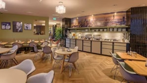 Restaurante com piso de madeira, mesas redondas e cadeiras modernas. Há um balcão com um mural da paisagem urbana na parede ao fundo.