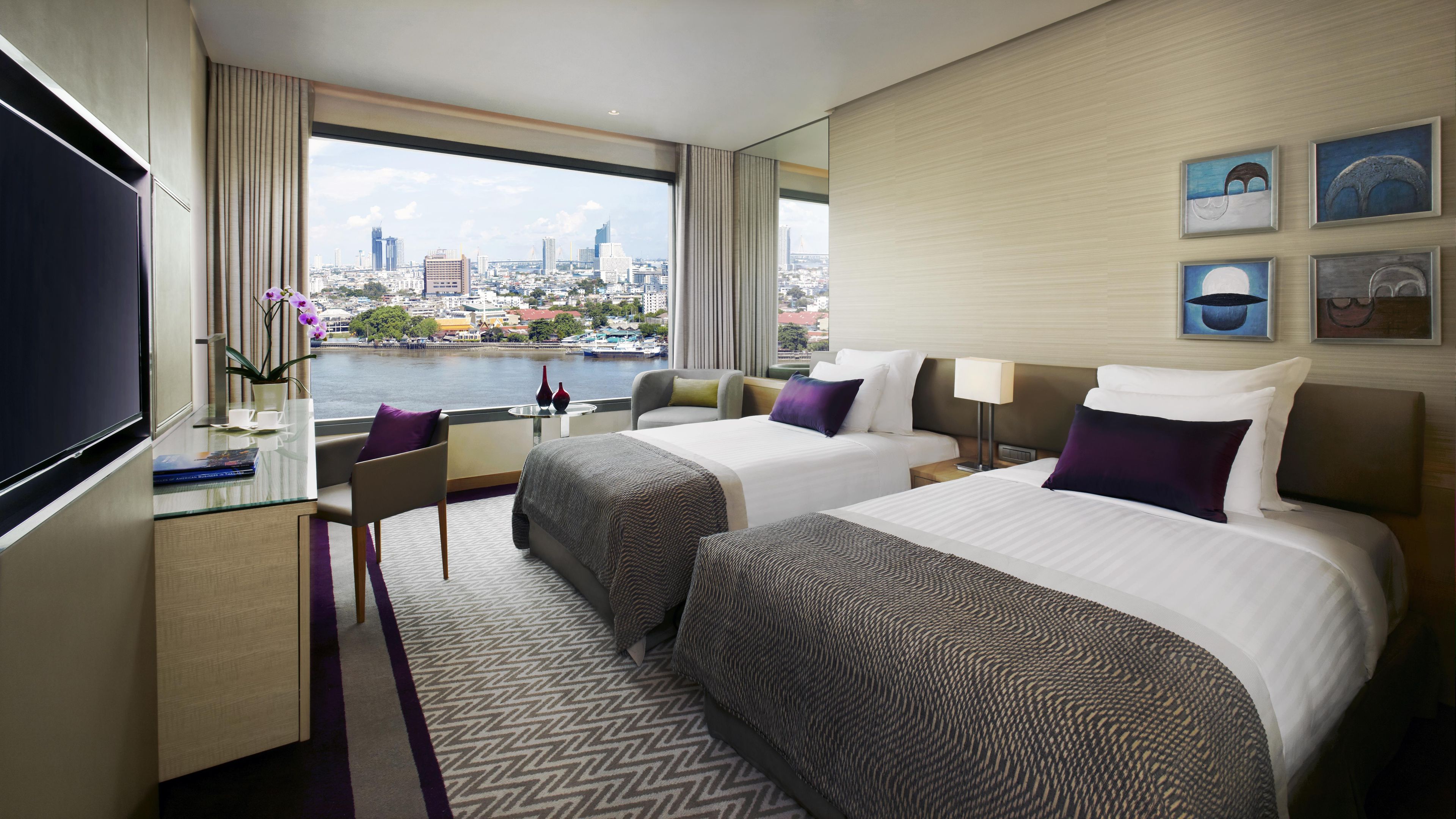 Quarto de hotel com duas camas, uma escrivaninha e televisão, e vista para a paisagem urbana.