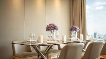 Mesa de jantar posta com pratos brancos, copos e velas, acompanhada por cadeiras com vista para a cidade.