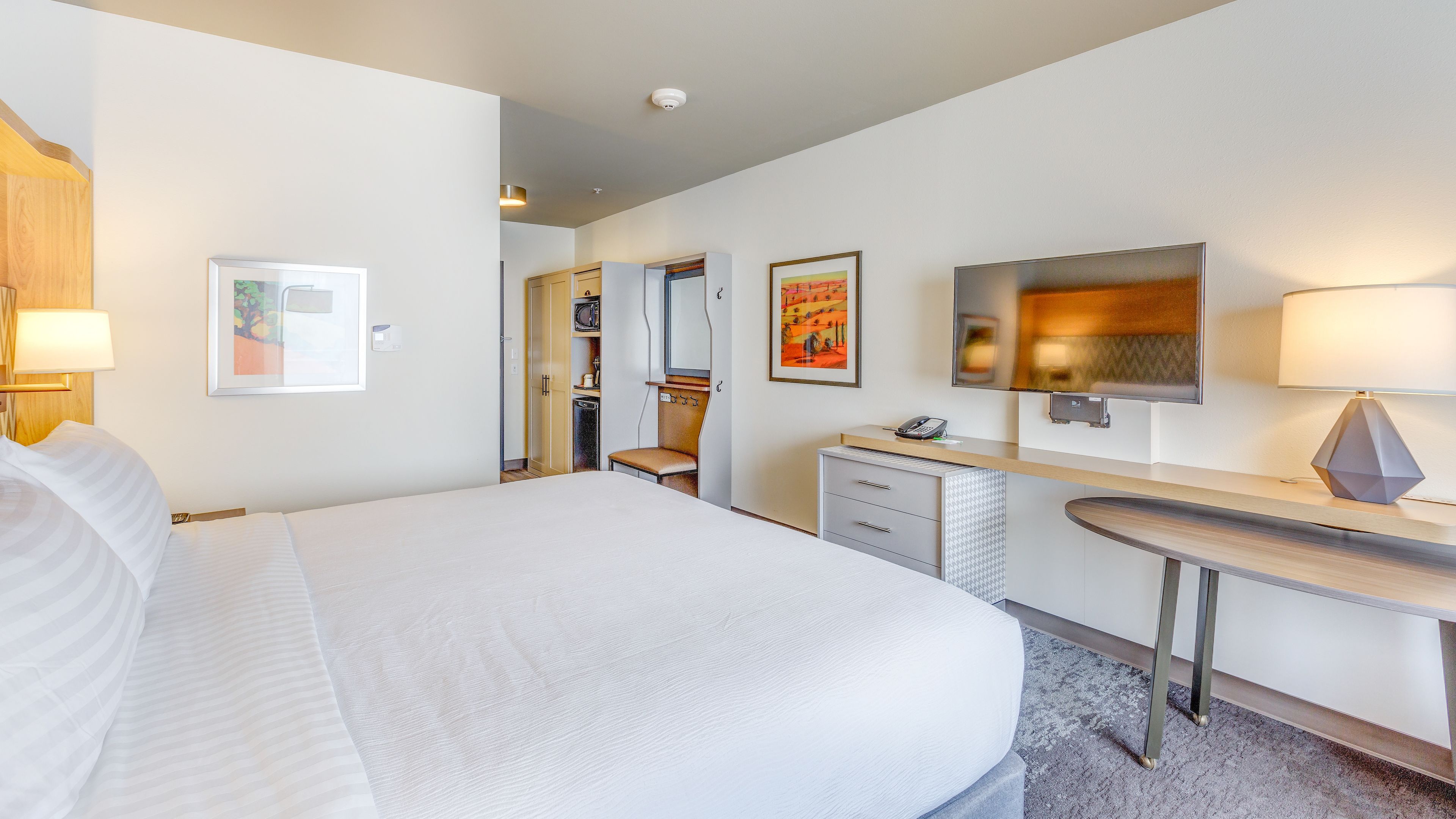 Quarto de hotel com uma cama grande, uma escrivaninha com abajur, telefone e espelho.