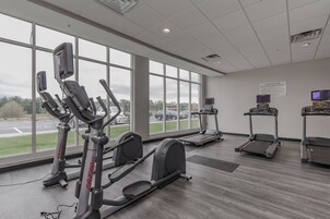 Uma academia com equipamentos de cardio, amplas janelas e uma placa com as regras do centro de fitness.
