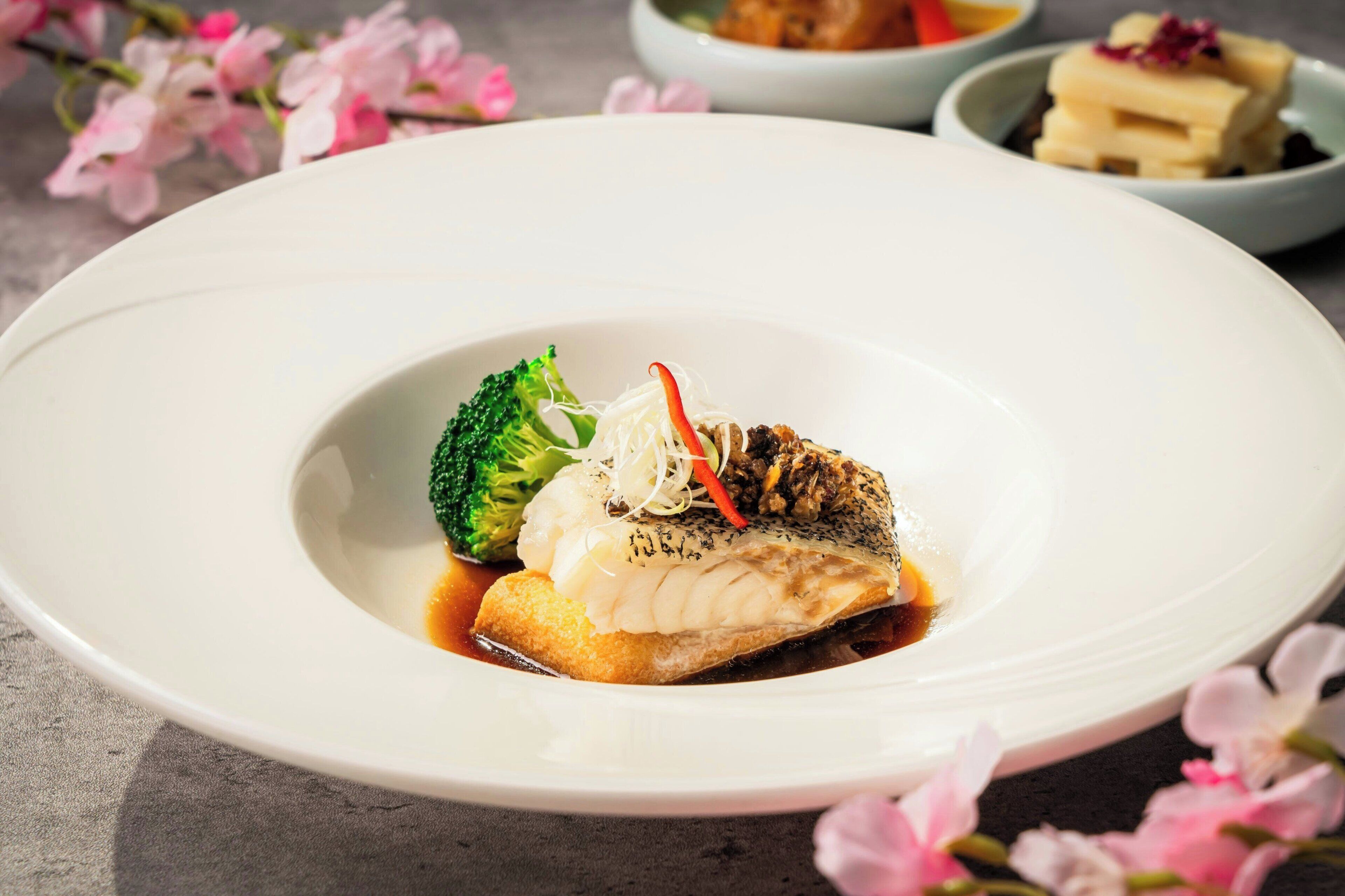 Um prato branco com um filé de peixe, brócolis e molho.