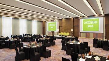 Uma sala de conferências com várias mesas e cadeiras, uma tela grande exibindo 'Courtyard Marriott' e um palco com um púlpito.