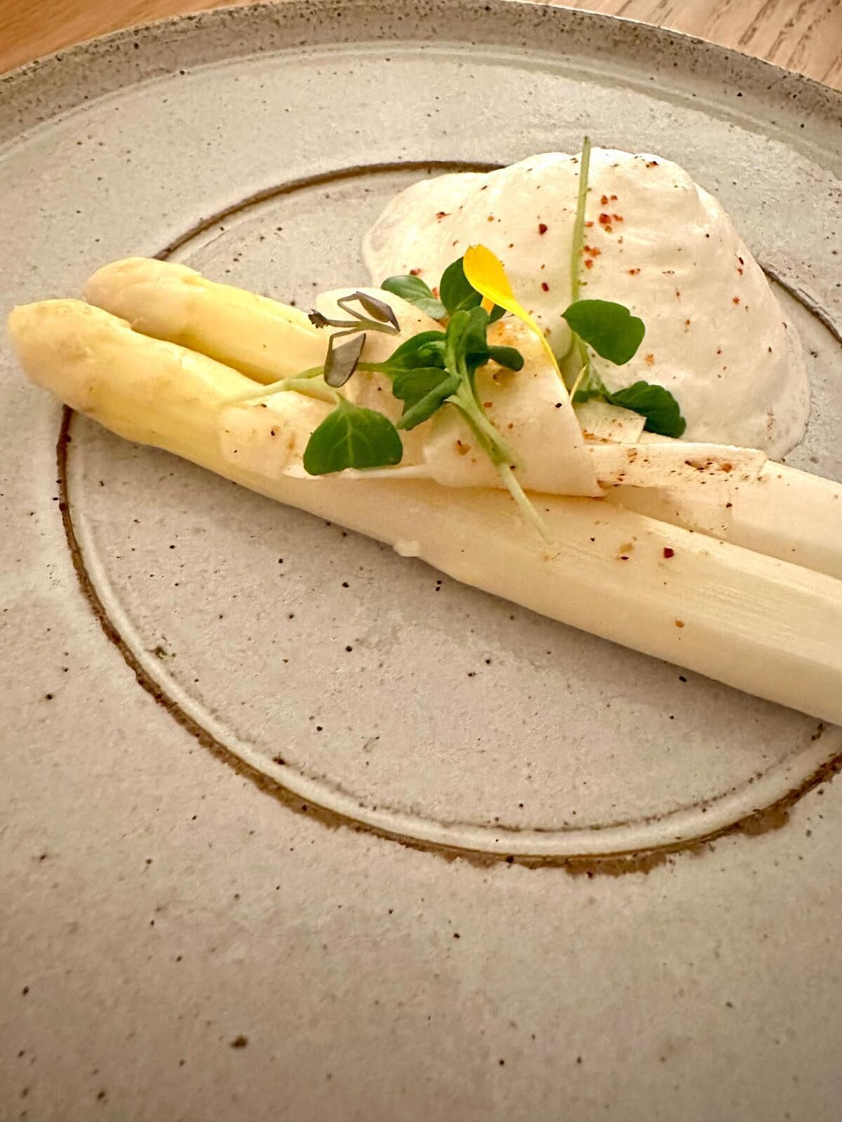 Um prato com molho branco, folhas verdes e flores amarelas sobre um aspargo branco.