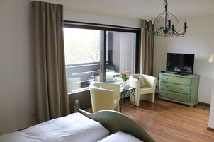 Quarto de hotel com uma cama, televisão, cômoda verde, cadeira e mesa com um vaso de flores.