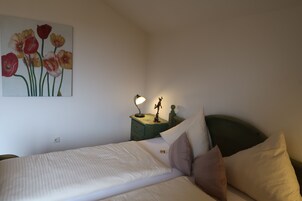 Uma cama bem arrumada com manta listrada, cabeceira verde e mesa de cabeceira com abajur e uma pequena estátua.