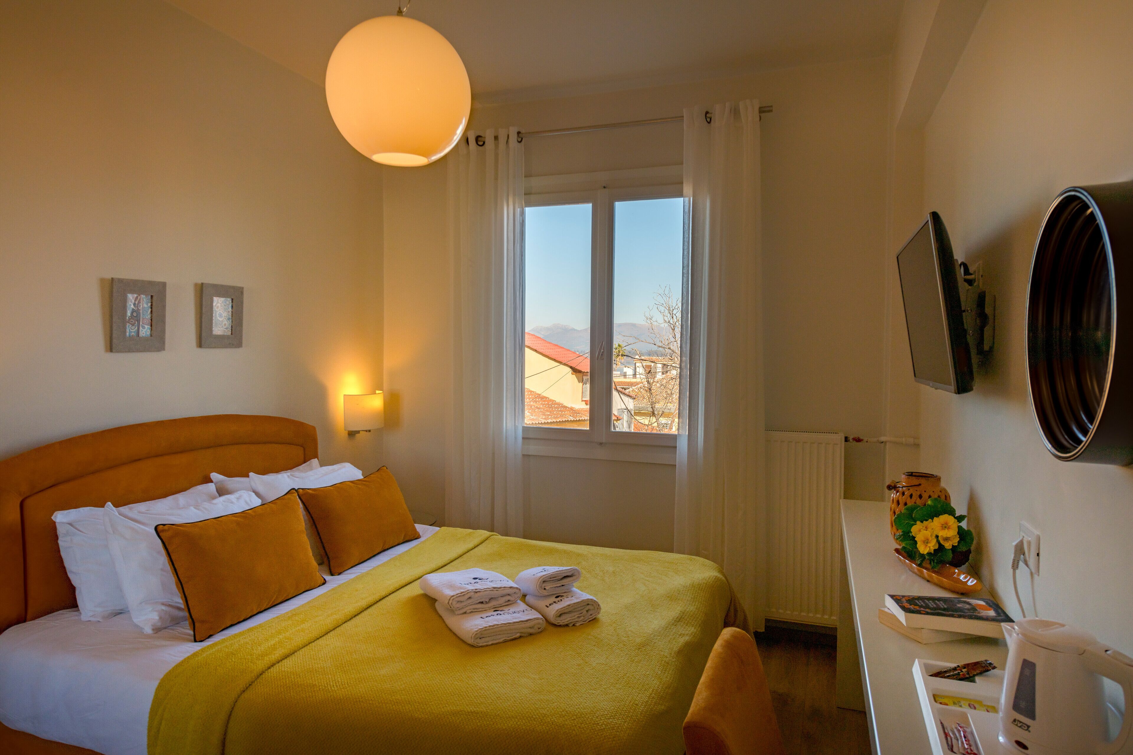 Quarto de hotel com cama, janela com cortinas, televisão fixada na parede e radiador.